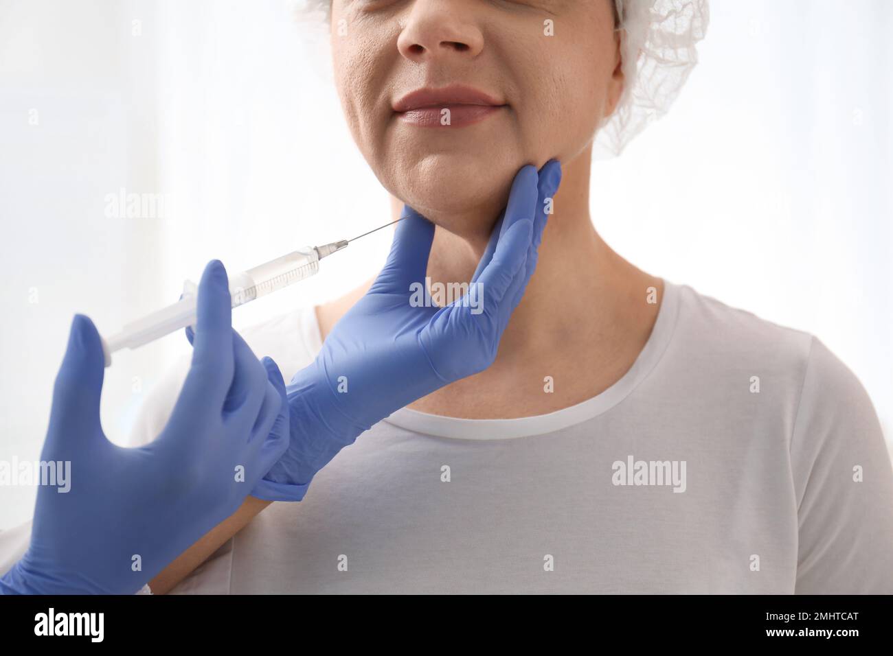 Mature woman with double chin receiving injection in clinic, closeup ...