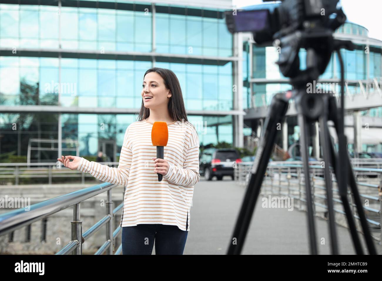 Young female journalist with microphone working on city street Stock ...