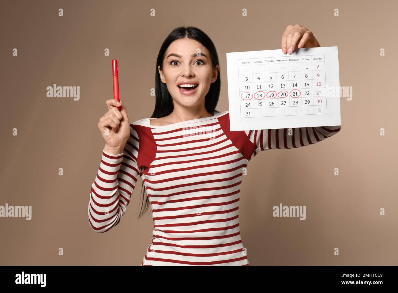 Young woman holding calendar with marked menstrual cycle days on beige ...