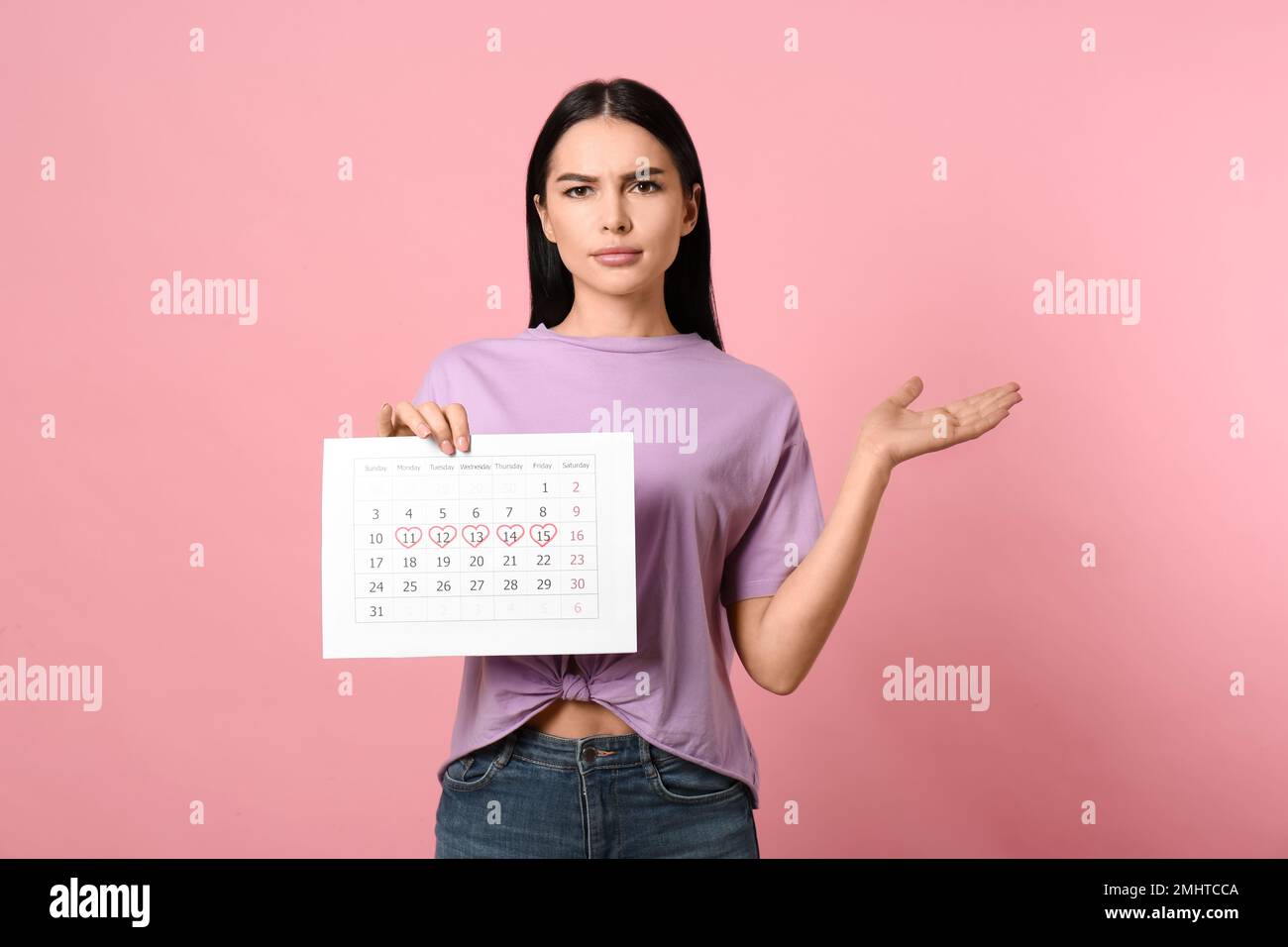 Young woman holding calendar with marked menstrual cycle days on pink ...