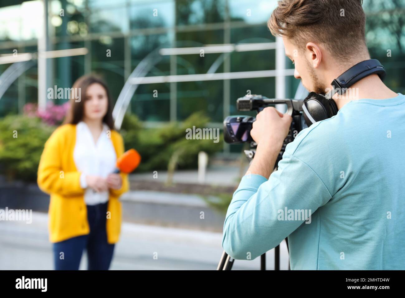 Young journalist and video operator working on city street. Space for ...