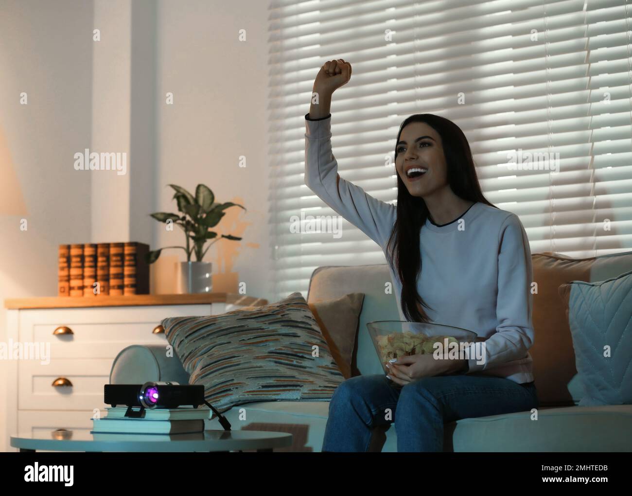 Emotional young woman watching TV using video projector at home Stock ...