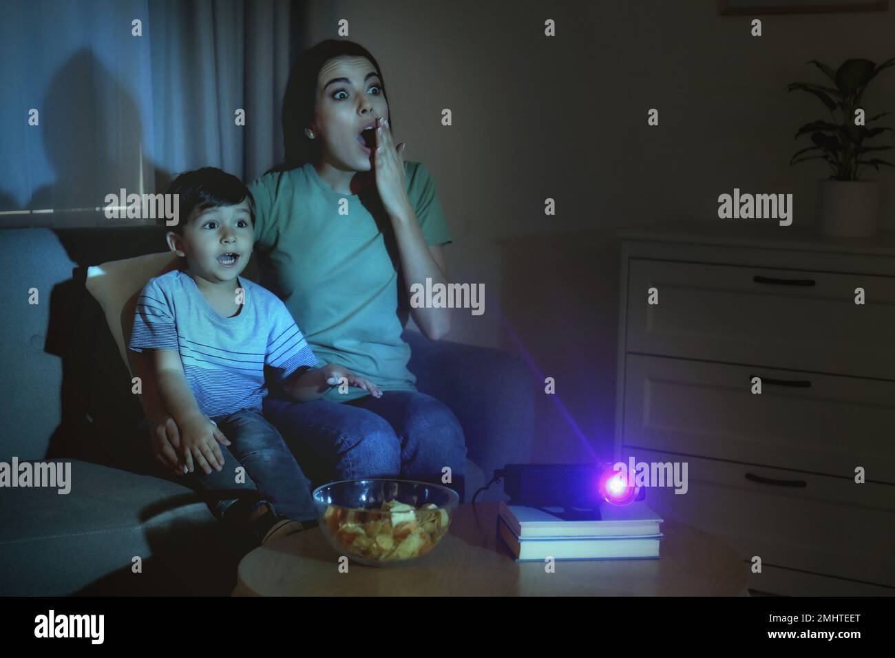 Emotional young woman and her son watching movie using video projector ...