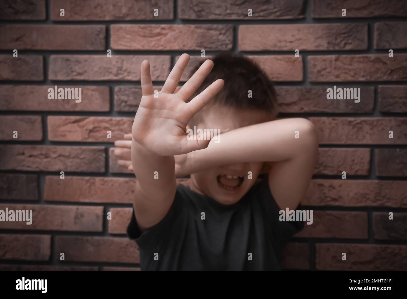 Scared little boy closing eyes with hand near brick wall. Child in ...