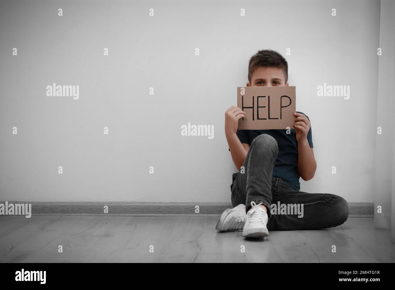 Sad little boy with sign HELP sitting on floor indoors, space for text ...
