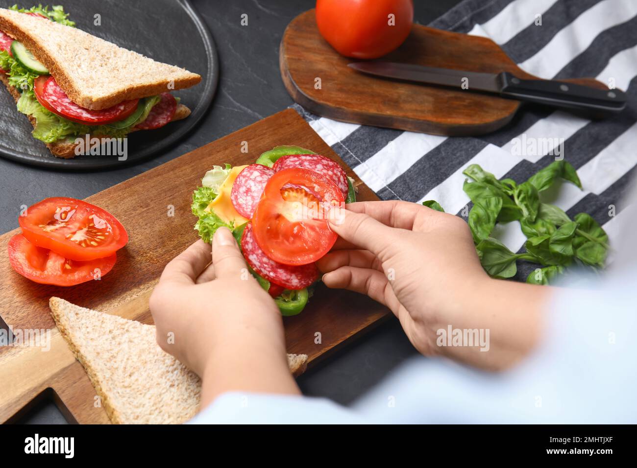 Woman adding tomato to sandwich at black table, closeup Stock Photo - Alamy