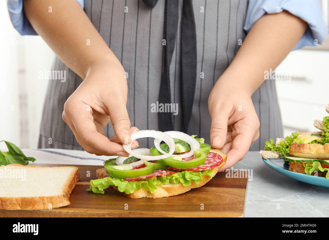 Woman adding onion to tasty sandwich at light grey marble table ...