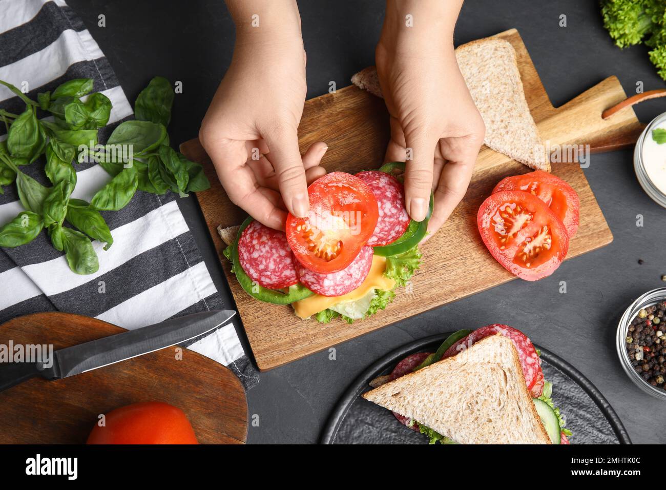 Woman adding tomato to sandwich at black table, top view Stock Photo ...