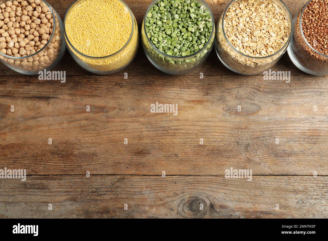 Glass jars with different types of groats on wooden table, flat lay ...