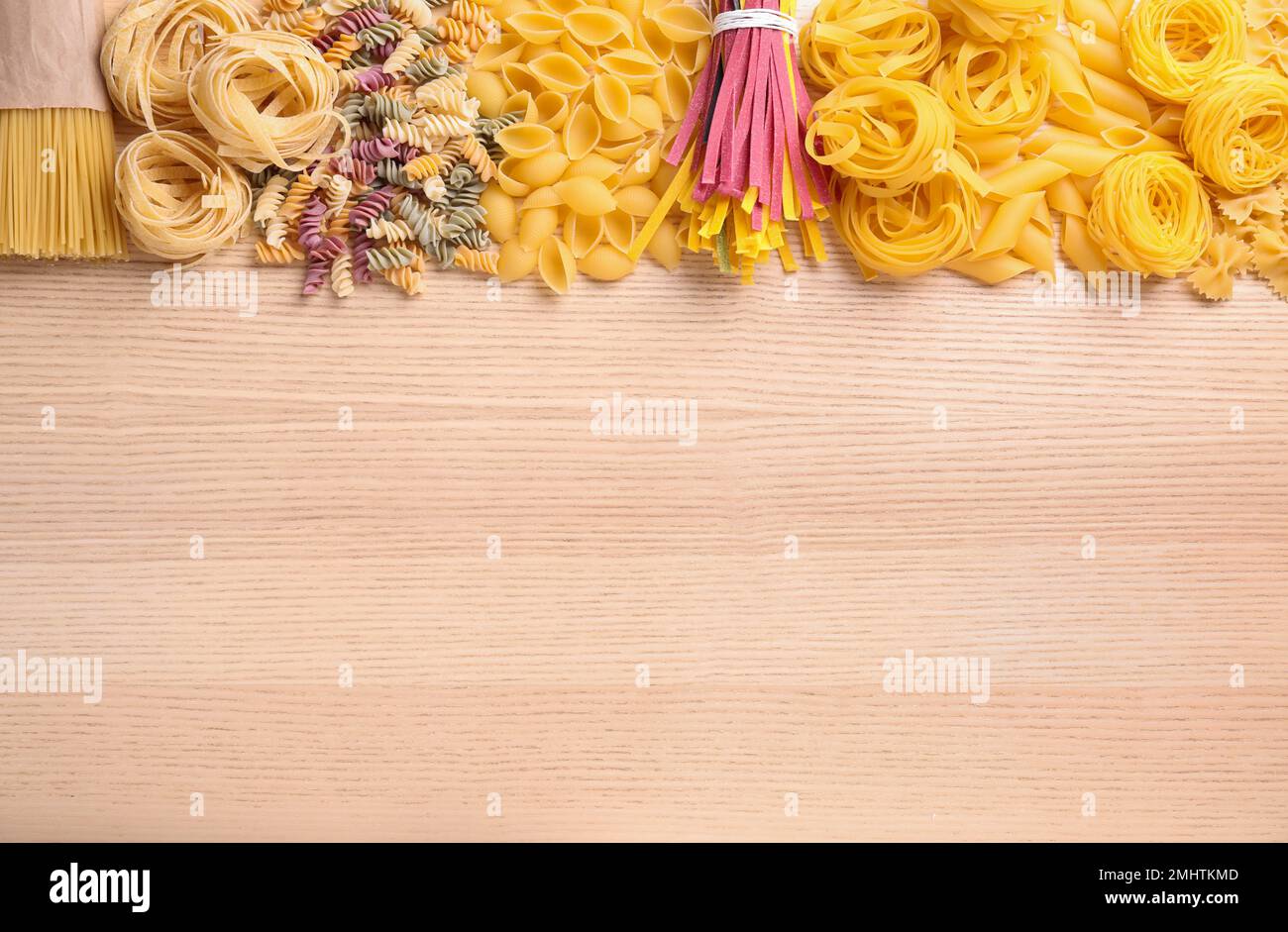 Different types of pasta on wooden table, flat lay. Space for text ...