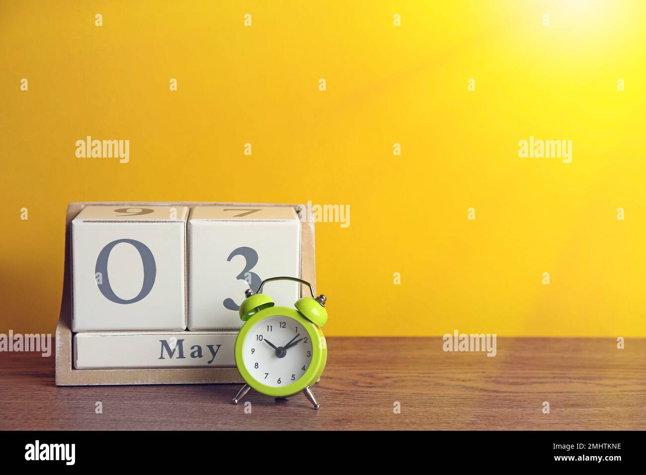 Wooden block calendar and alarm clock on table against yellow ...