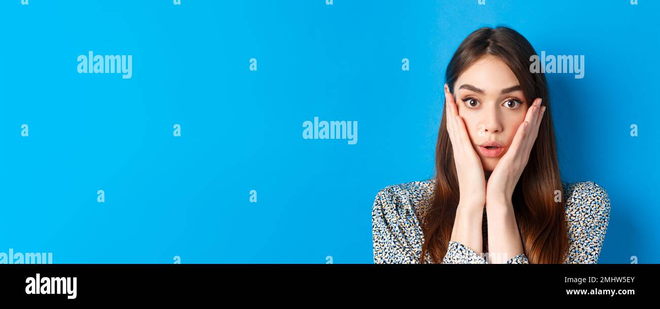 Close-up portrait of surprised cute woman holding hands on cheeks and ...