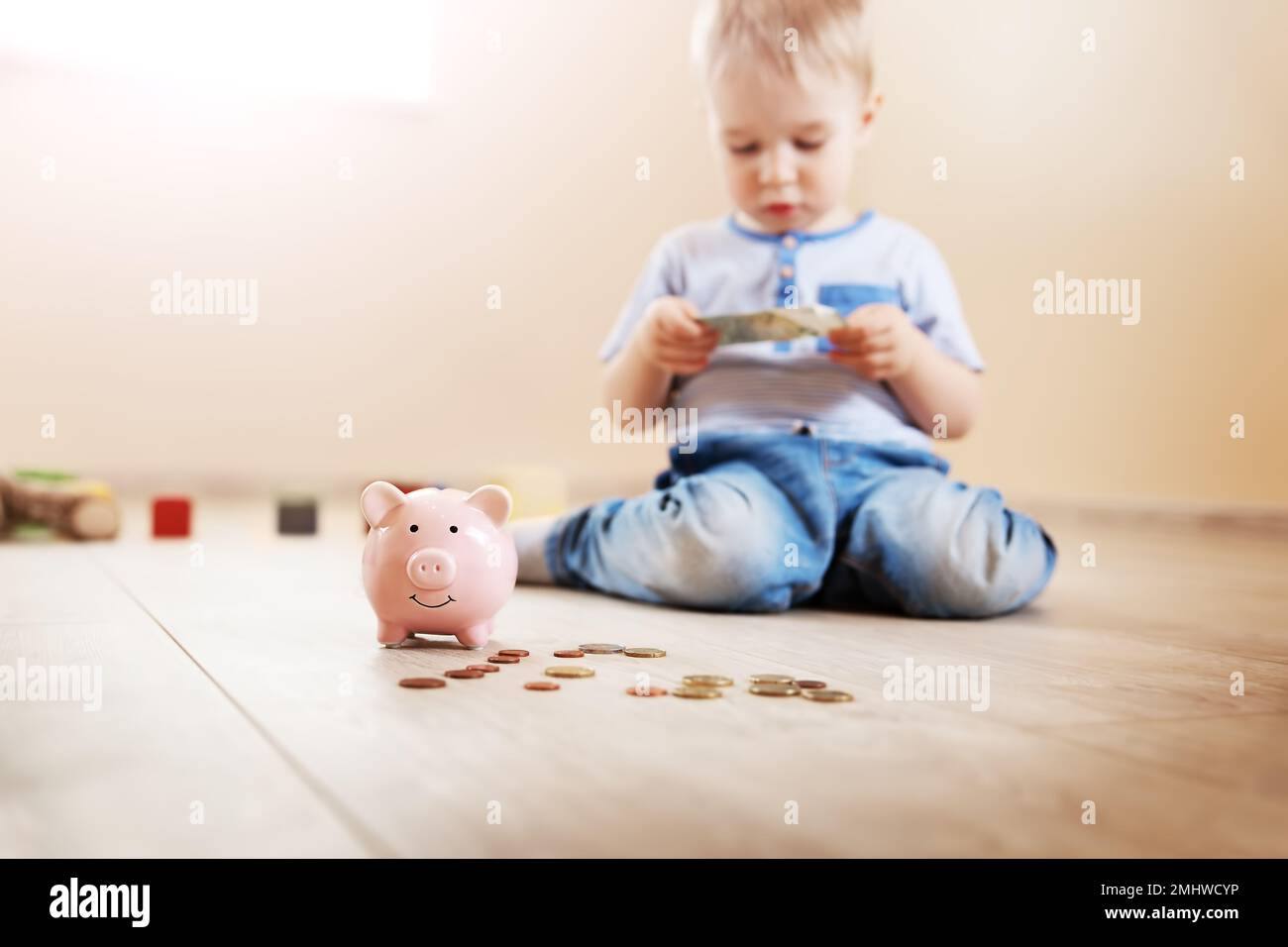 Cute boy sitting on the floor indoor and inserting euro coins in ...
