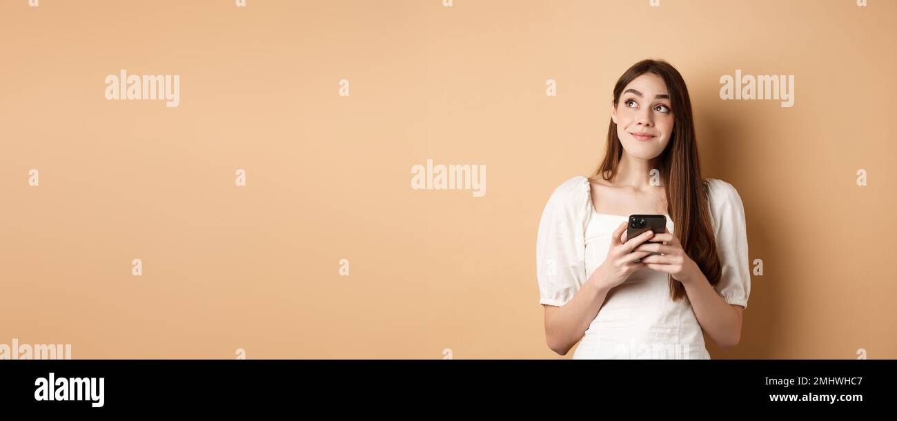 Romantic girl thinking with phone, looking aside and smiling dreamy ...