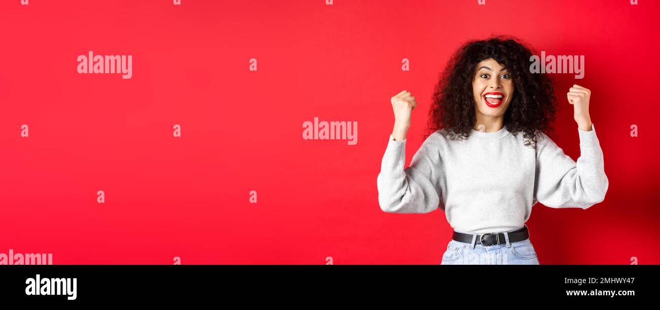 Cheerful lucky woman with curly hair, winning prize and scream yes with ...