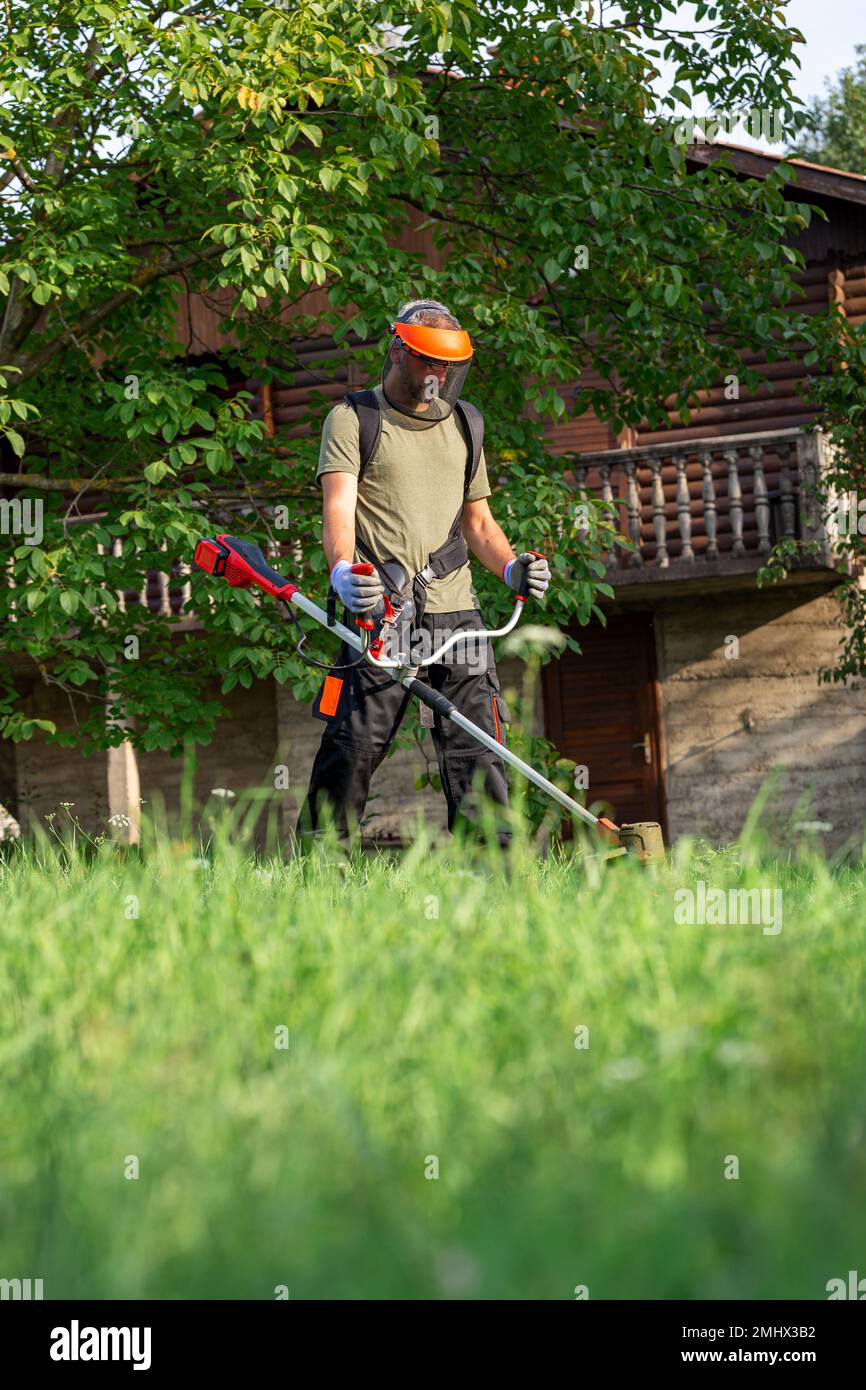 Side view of a gardener with electrical string grass cutter trimming ...