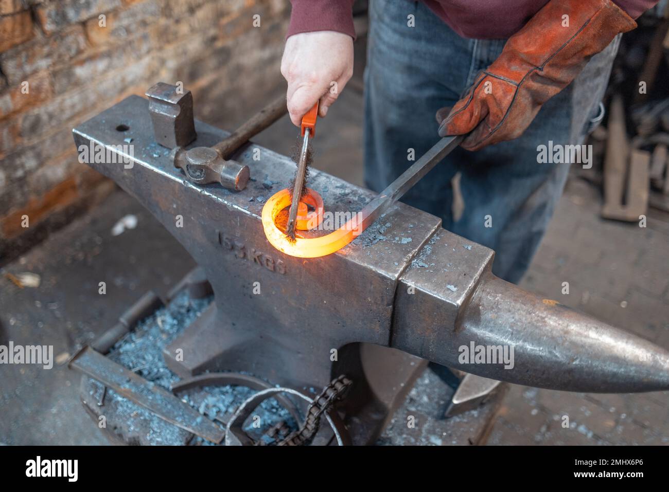 A man with a glove holding a hot iron hammer on an old anvil Stock ...