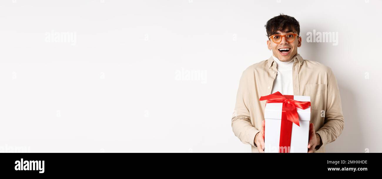 Surprised happy guy receiving a gift, holding present box and smiling ...