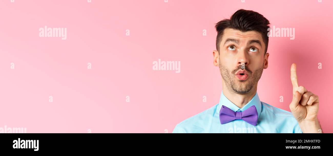 Intrigued young man in moustache, pointing finger and looking up at ...