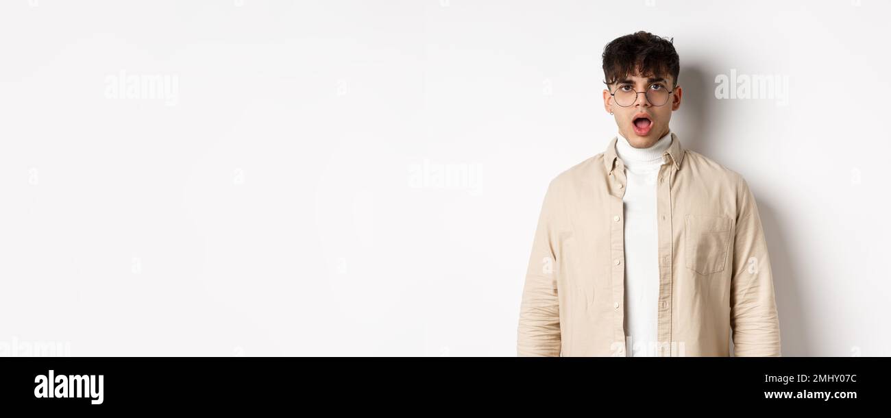 Portrait of shocked young man in glasses drop jaw, open mouth and stare ...
