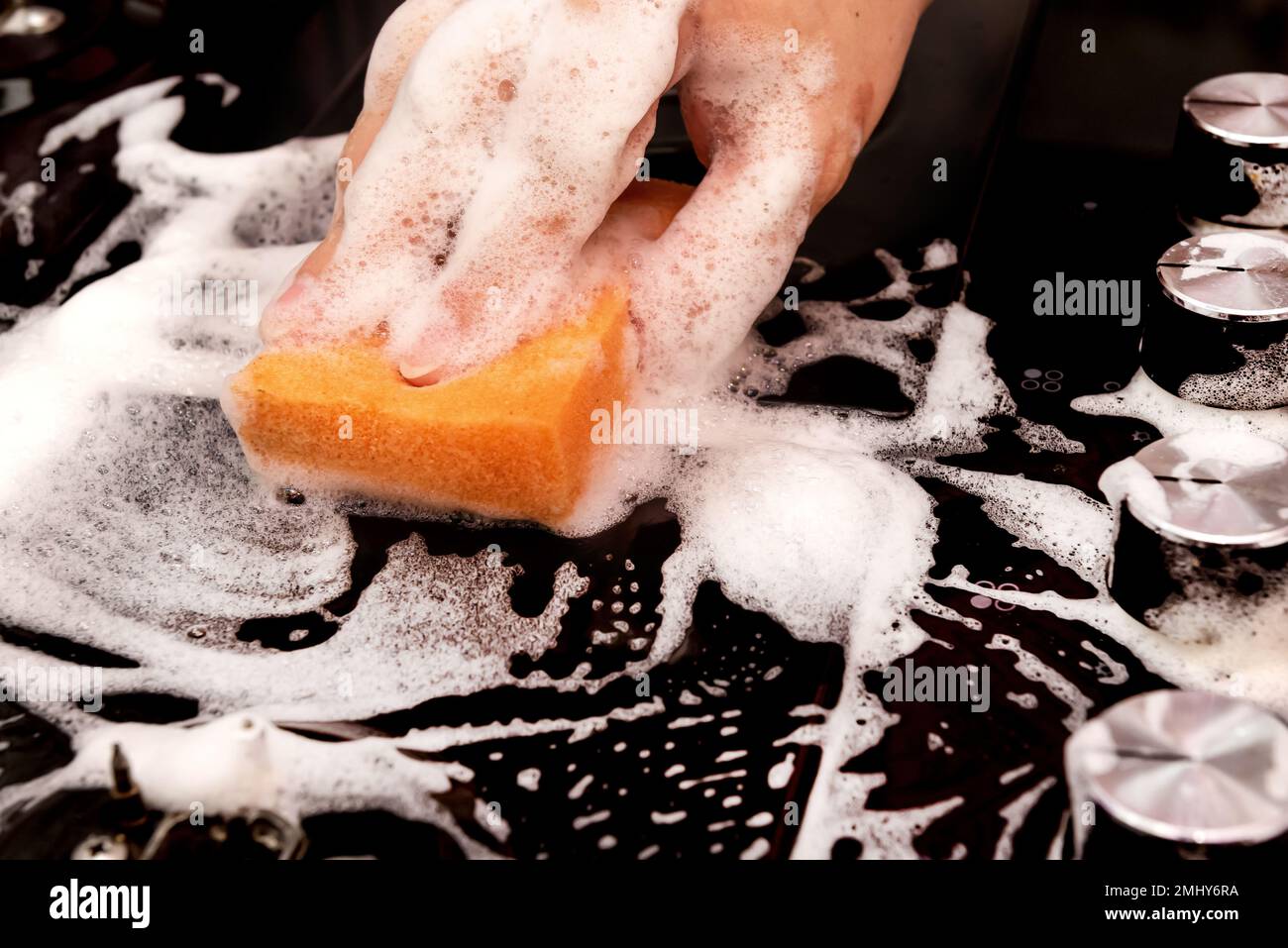 A hand with a yellow wash sponge washes the very dirty greasy surface ...