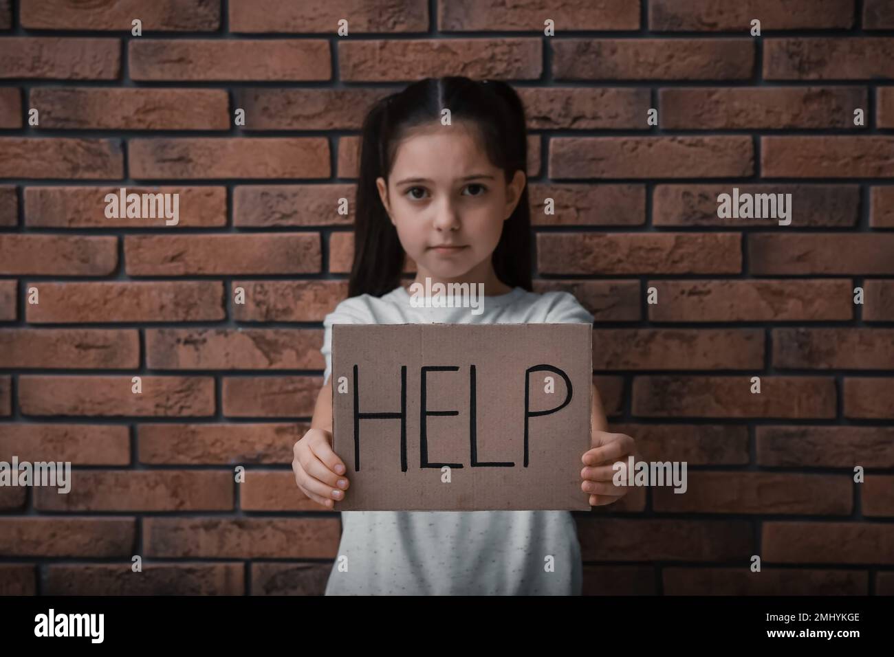 Sad little girl with sign HELP near brick wall. Child in danger Stock ...