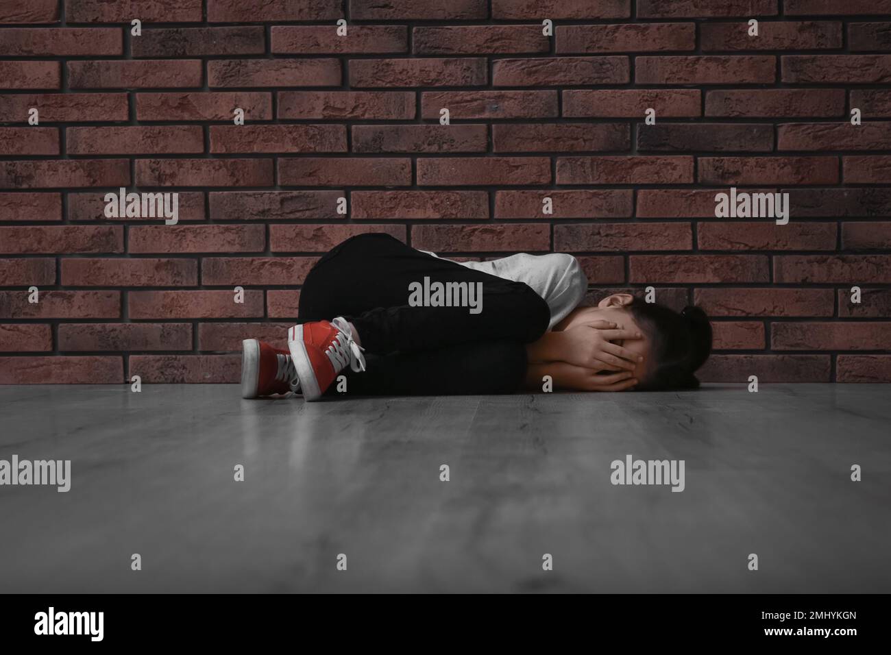 Sad little girl closing eyes with hands on floor near brick wall. Child ...