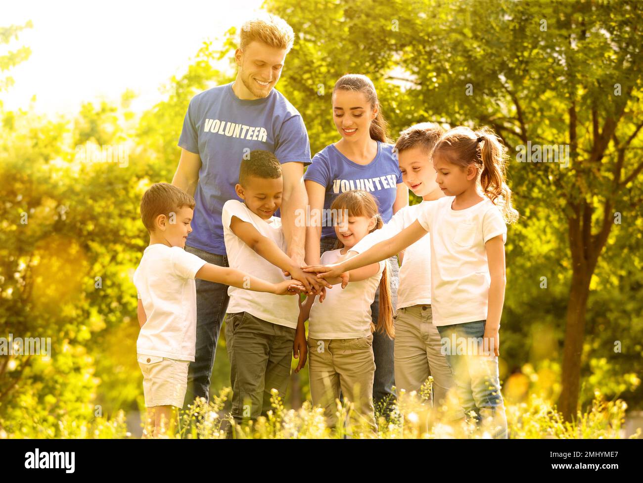 Group of kids joining hands with volunteers in park on sunny day Stock ...