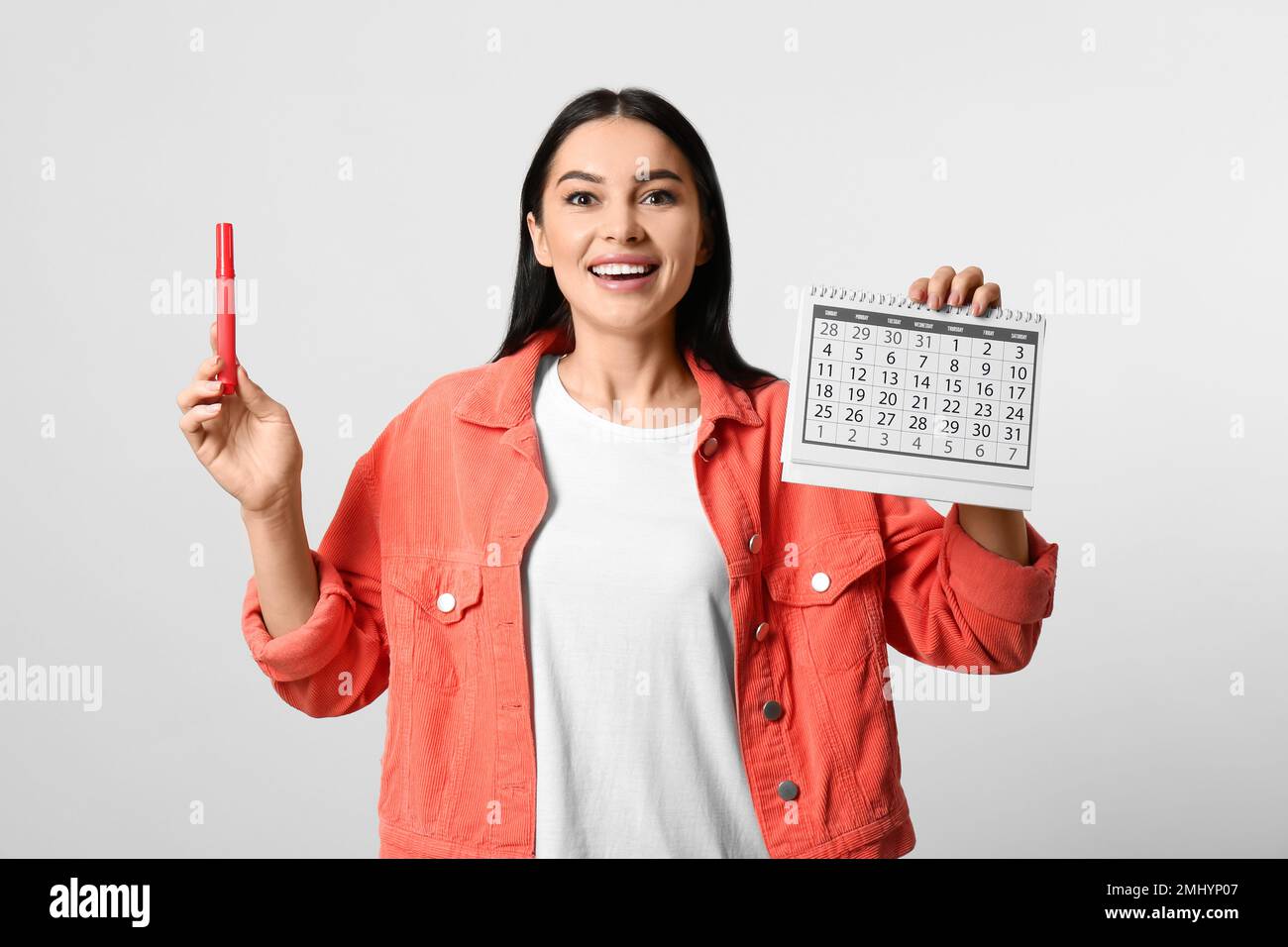 Young woman holding calendar with marked menstrual cycle days on light ...