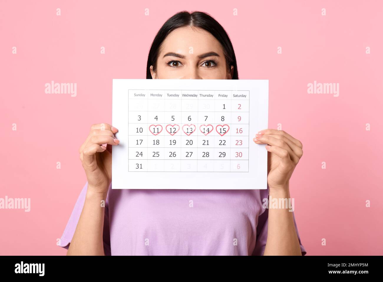 Young woman holding calendar with marked menstrual cycle days on pink ...