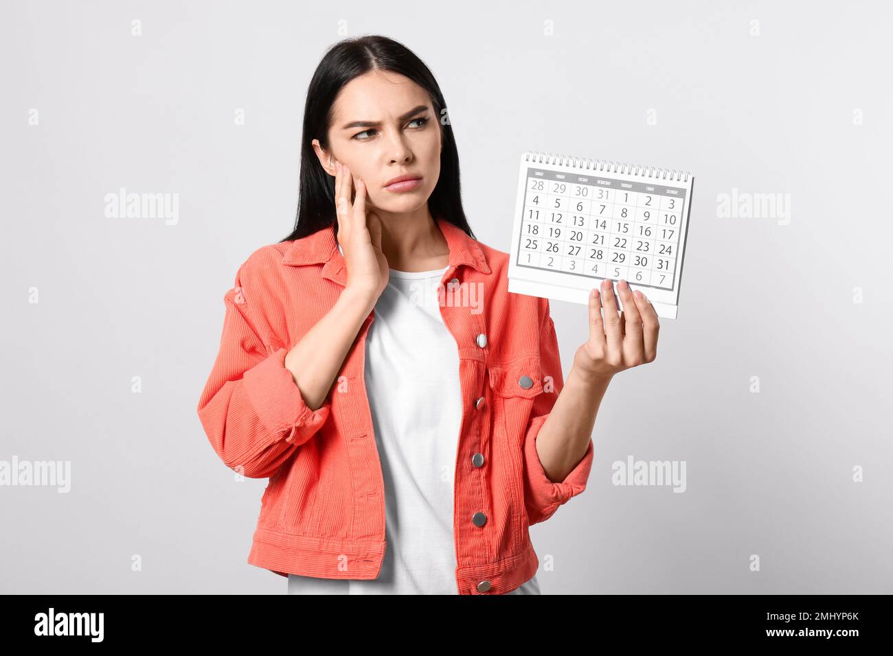 Pensive young woman holding calendar with marked menstrual cycle days ...