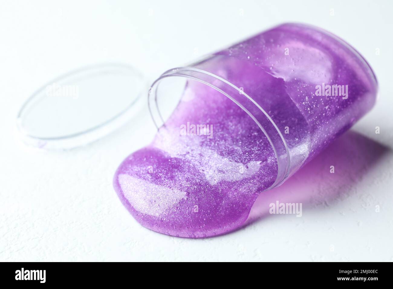 Overturned plastic container with purple slime on white background ...