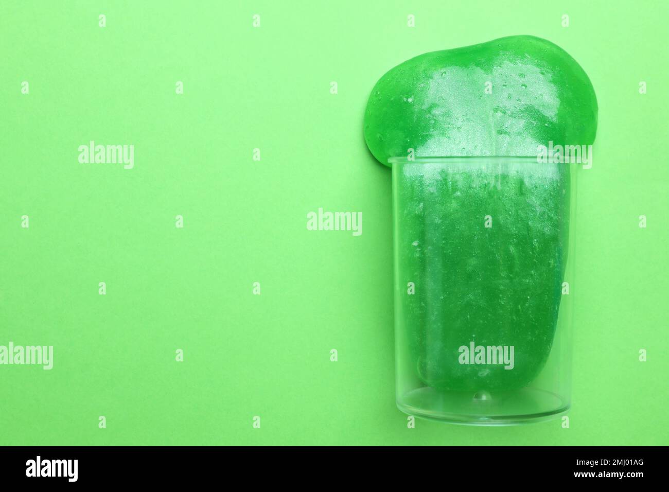 Overturned plastic container with bright slime on green background, top ...