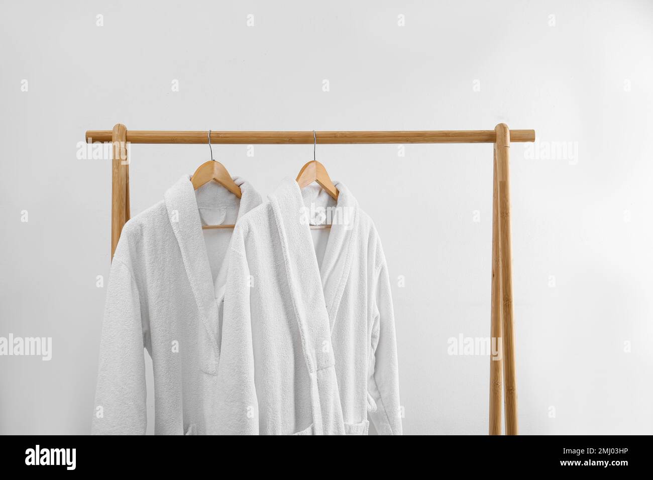 Fresh bathrobes hanging on rack near white wall Stock Photo - Alamy