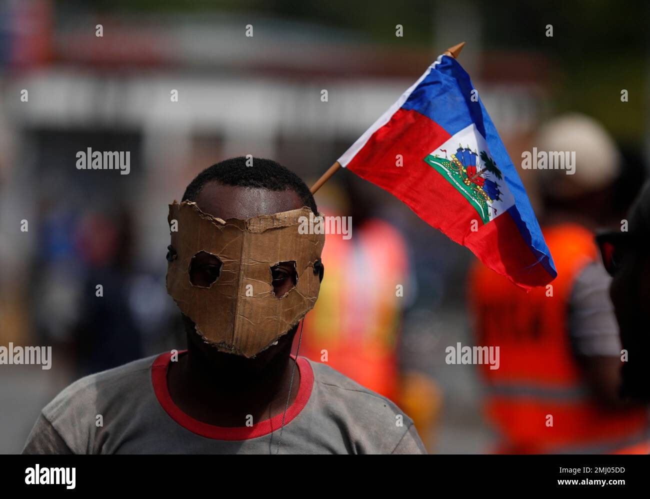 A protestor wears a Haitian flag tucked into his cardboard mask, in ...