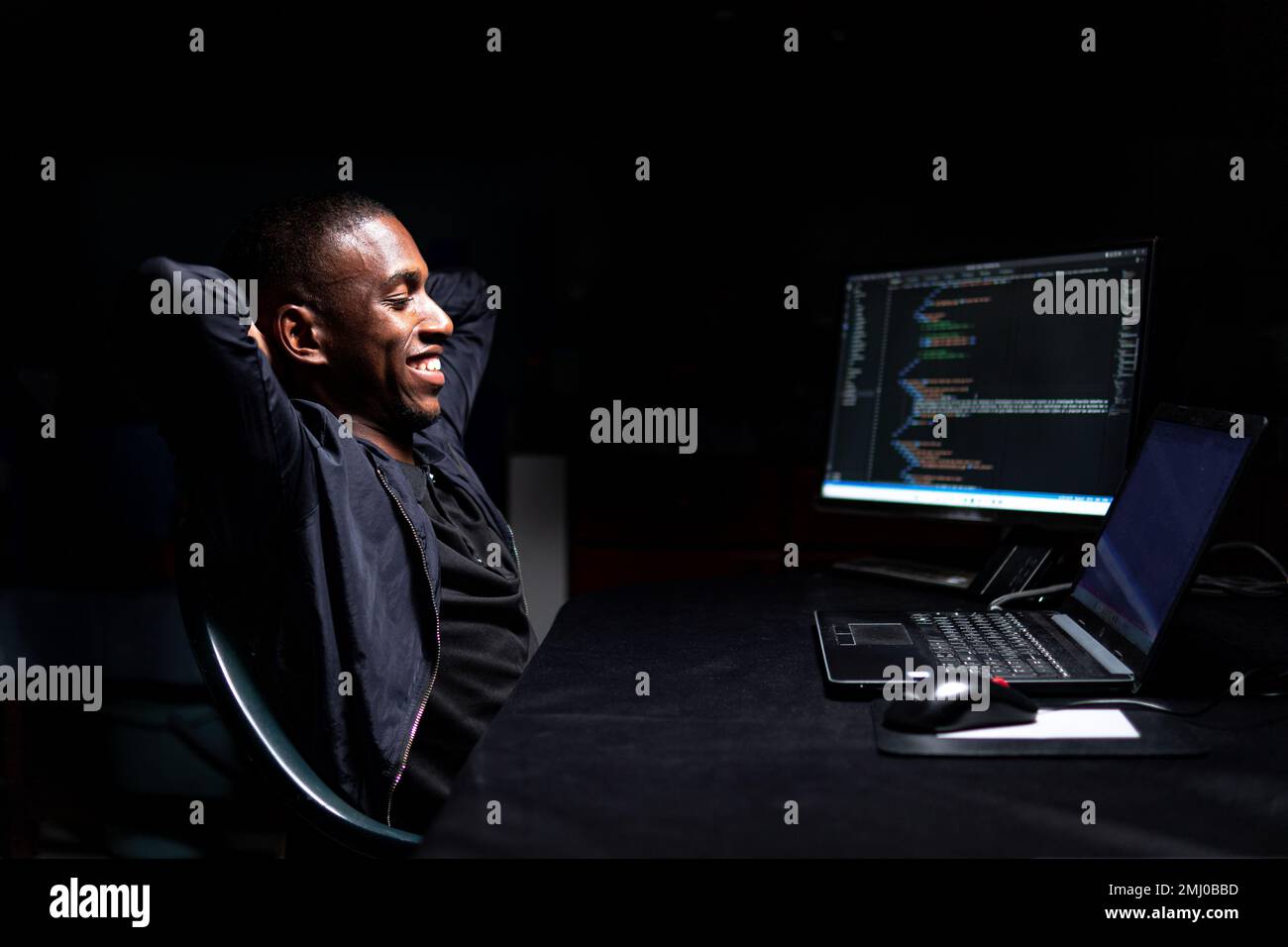 Relaxed male coder sitting back watching code in a dark room Stock ... Relaxed male coder sitting back watching code in a dark room Stock ...