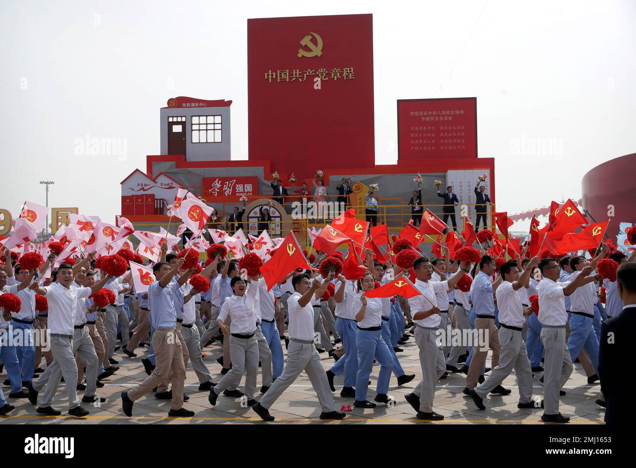 Participants wave Communist Party flags as they march next to a float ...
