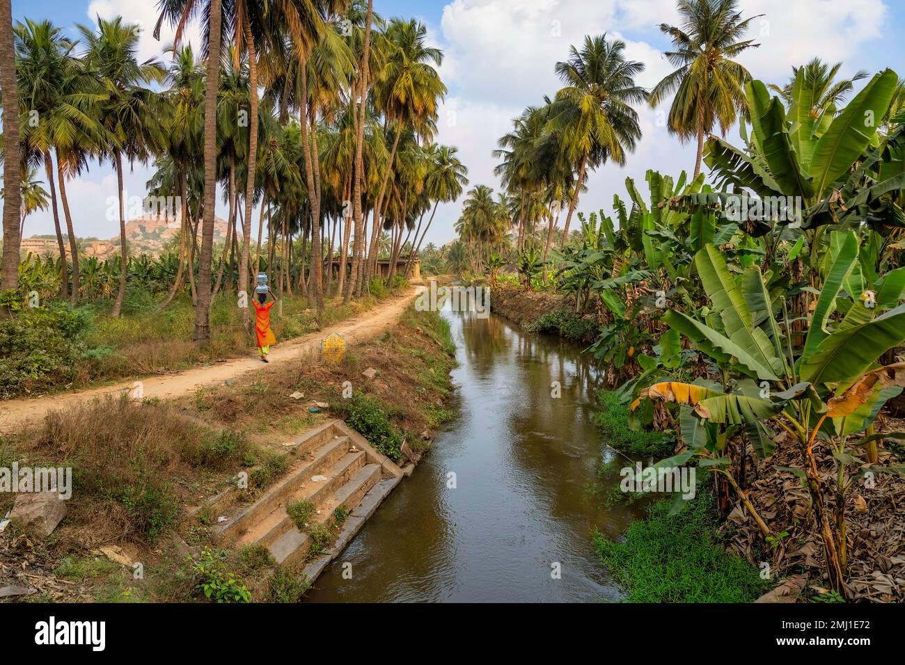 Indian village scene with small stream lined and unpaved village road ...
