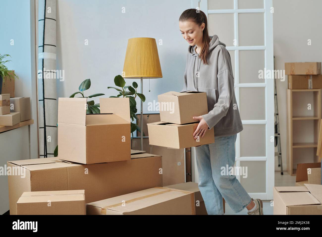 Young woman carrying packed boxes to the room during moving Stock Photo ...