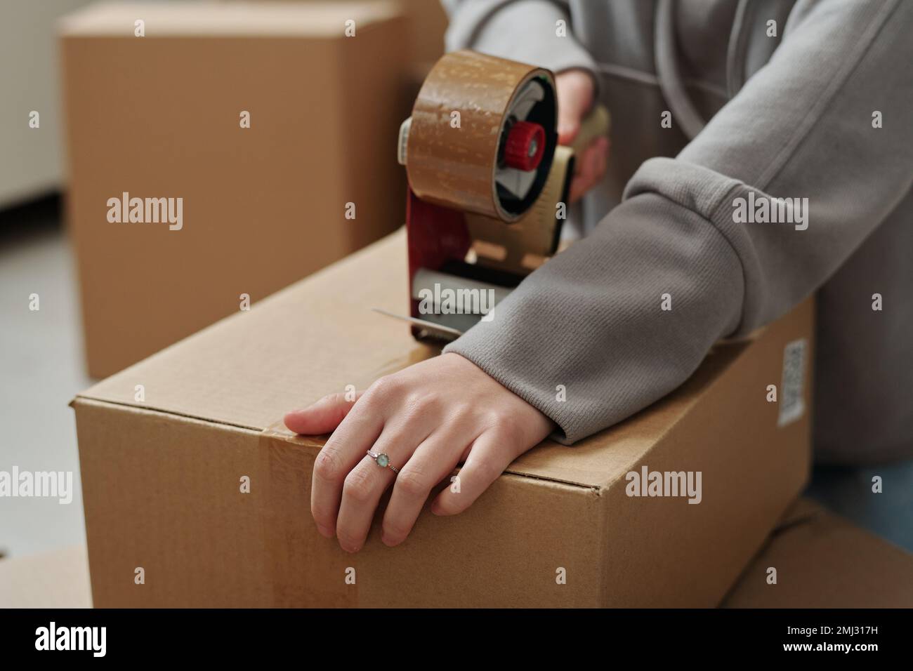 Close-up of young girl packing boxes with adhesive tape during ...