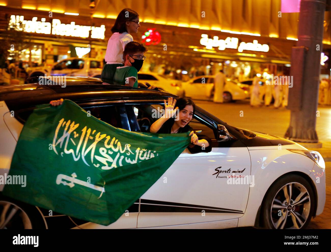 Saudis wave national flags as they hang out the window of a car during ...