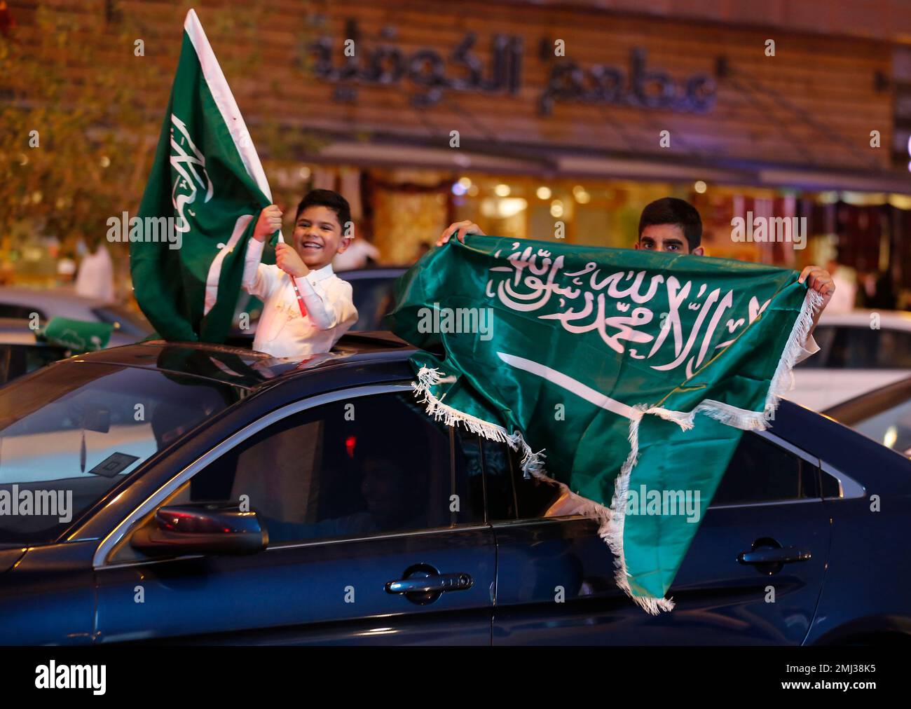Saudis wave national flags as they hang out the window of a car during ...
