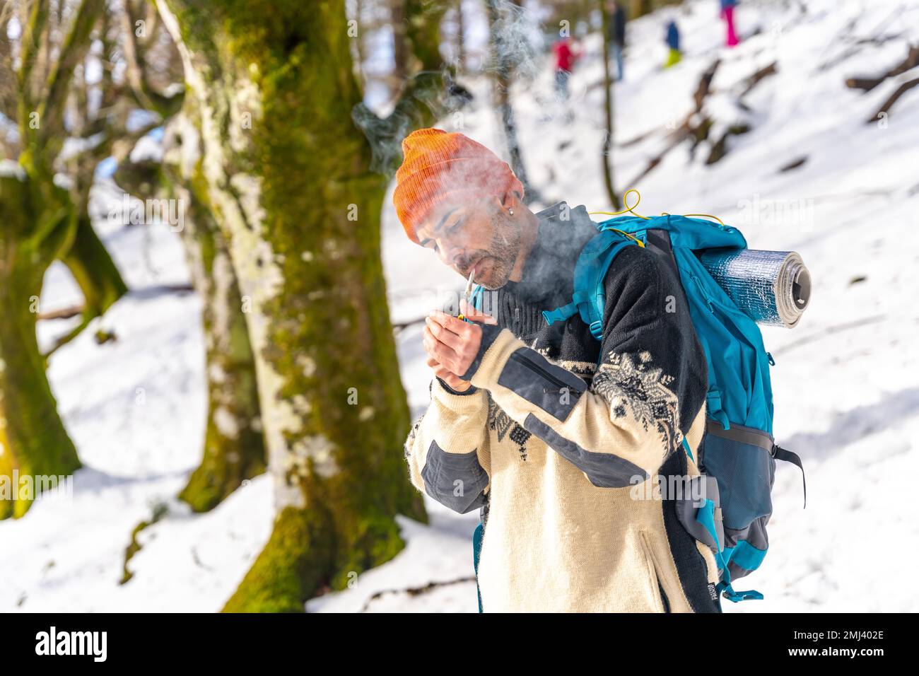 A man smoking lighting a cigarette with a lighter on a snowy mountain ...