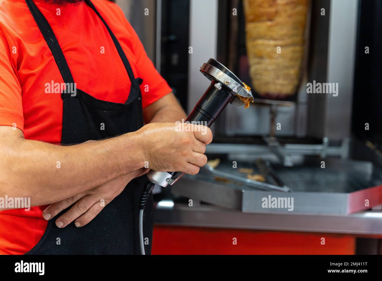 Chef of the kebab restaurant, using the electric tool to cut doner meat ...