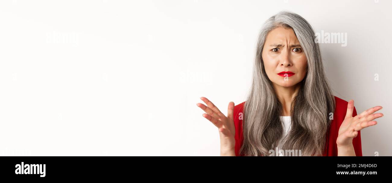 Close up of confused asian female manager with grey hair, wearing red ...