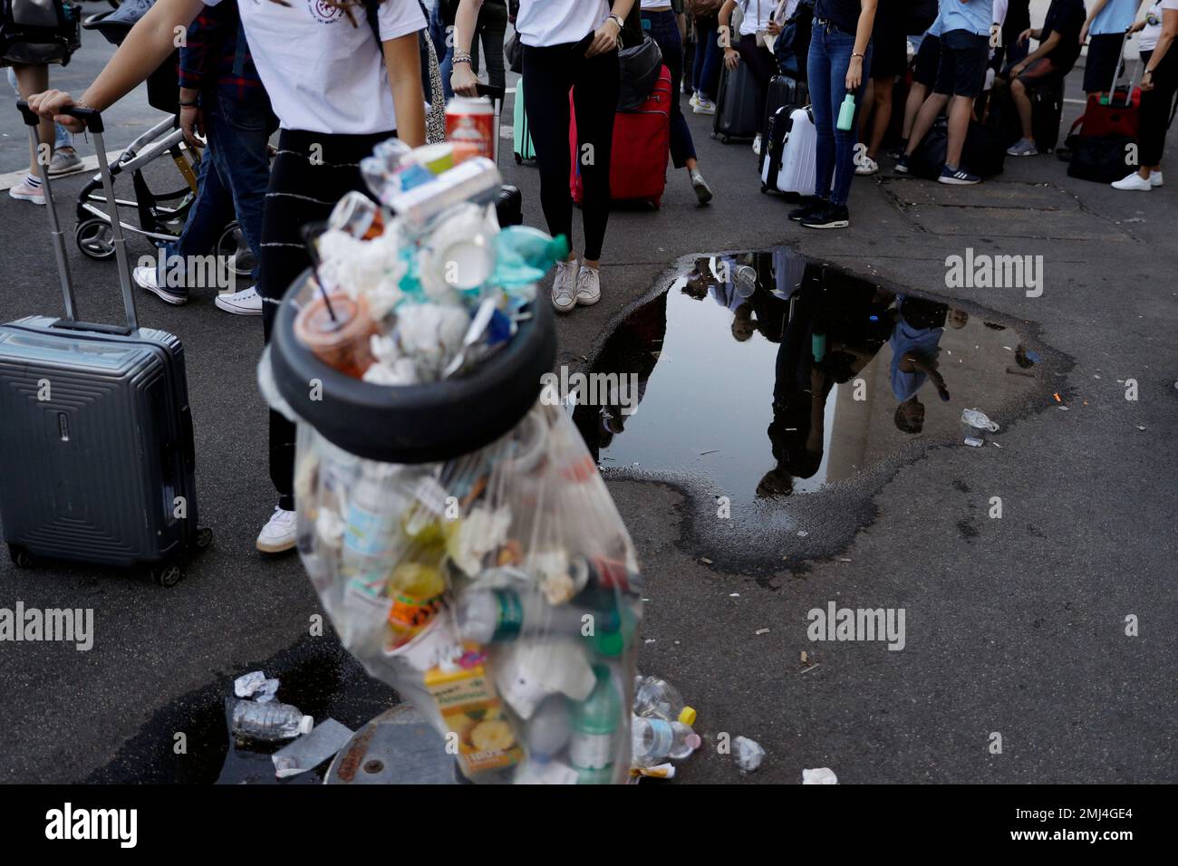 Tourists walk past a trash bin overflowing of waste in downtown Rome ...