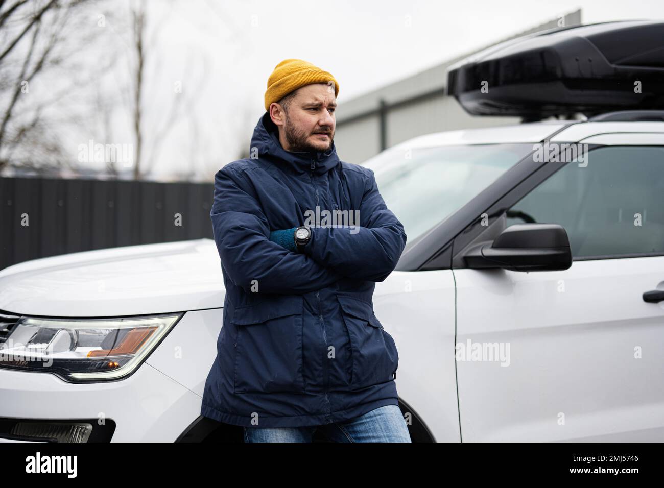 Man driver wear jacket and yellow hat against his american SUV car with ...