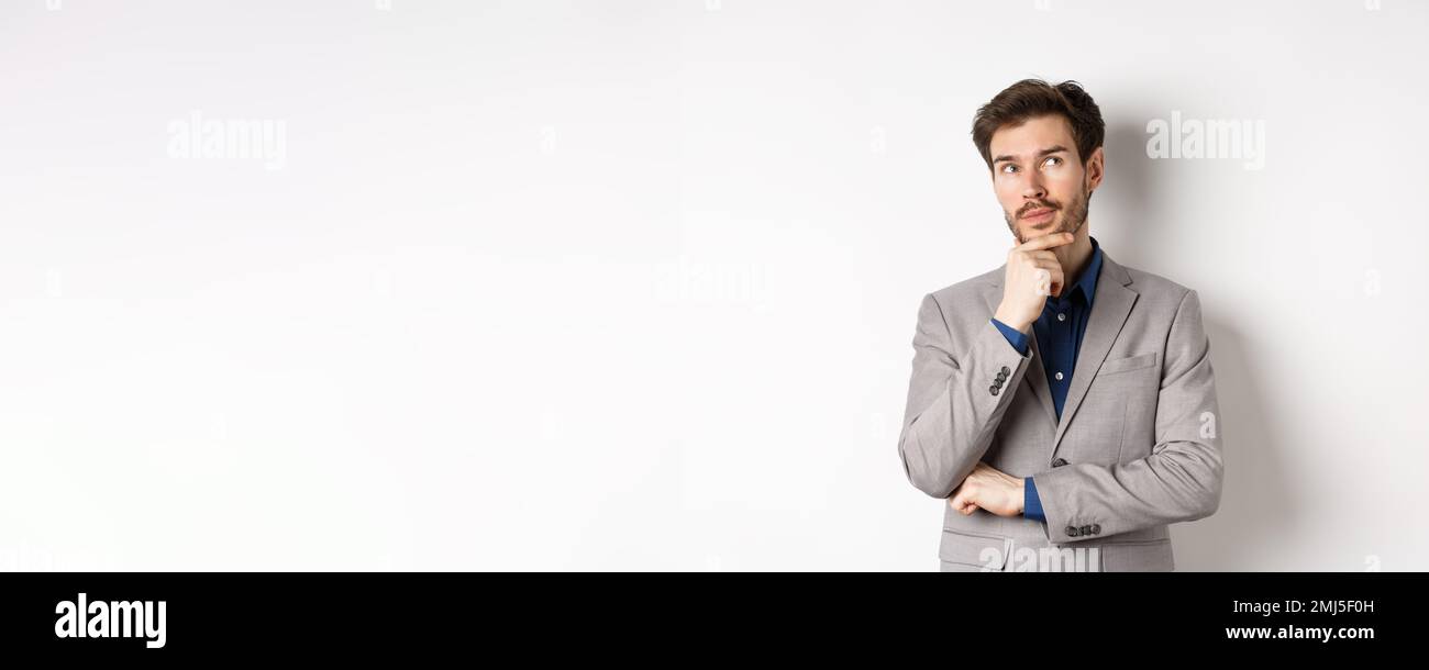 Pensive handsome man in suit looking up and thinking, making choice ...