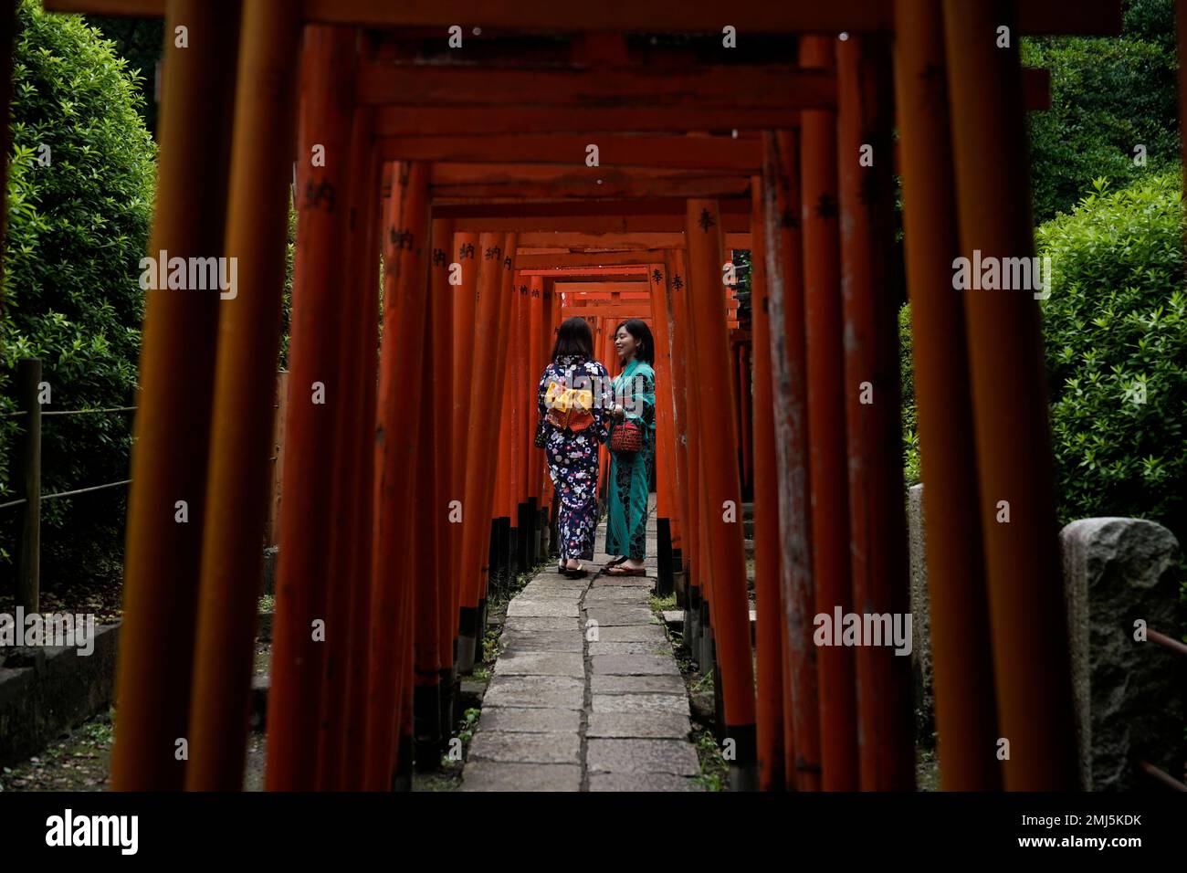 Two women wearing yukata walk through torii gates while visiting Nezu ...