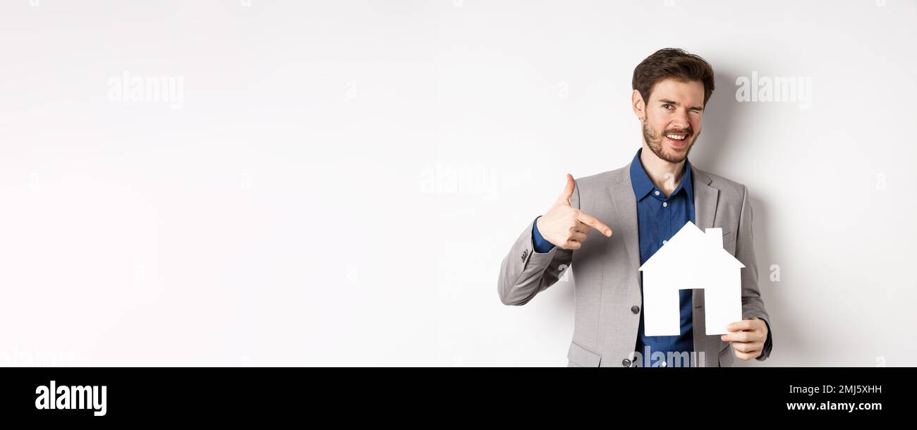 Real estate. Handsome businessman winking and pointing at paper house ...
